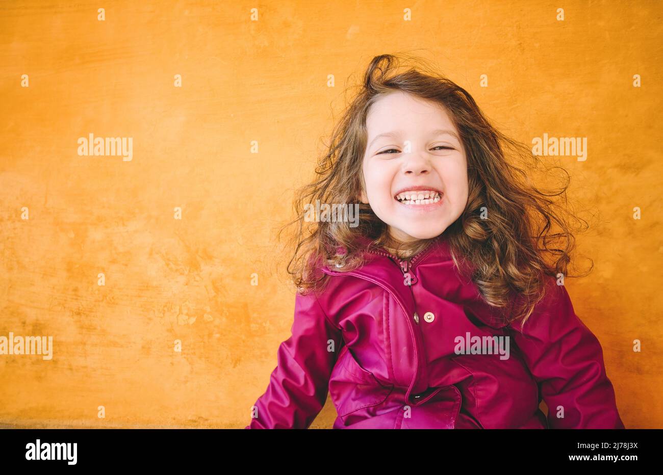 Young girl with a cheeky smile looking directly at the camera against a ...