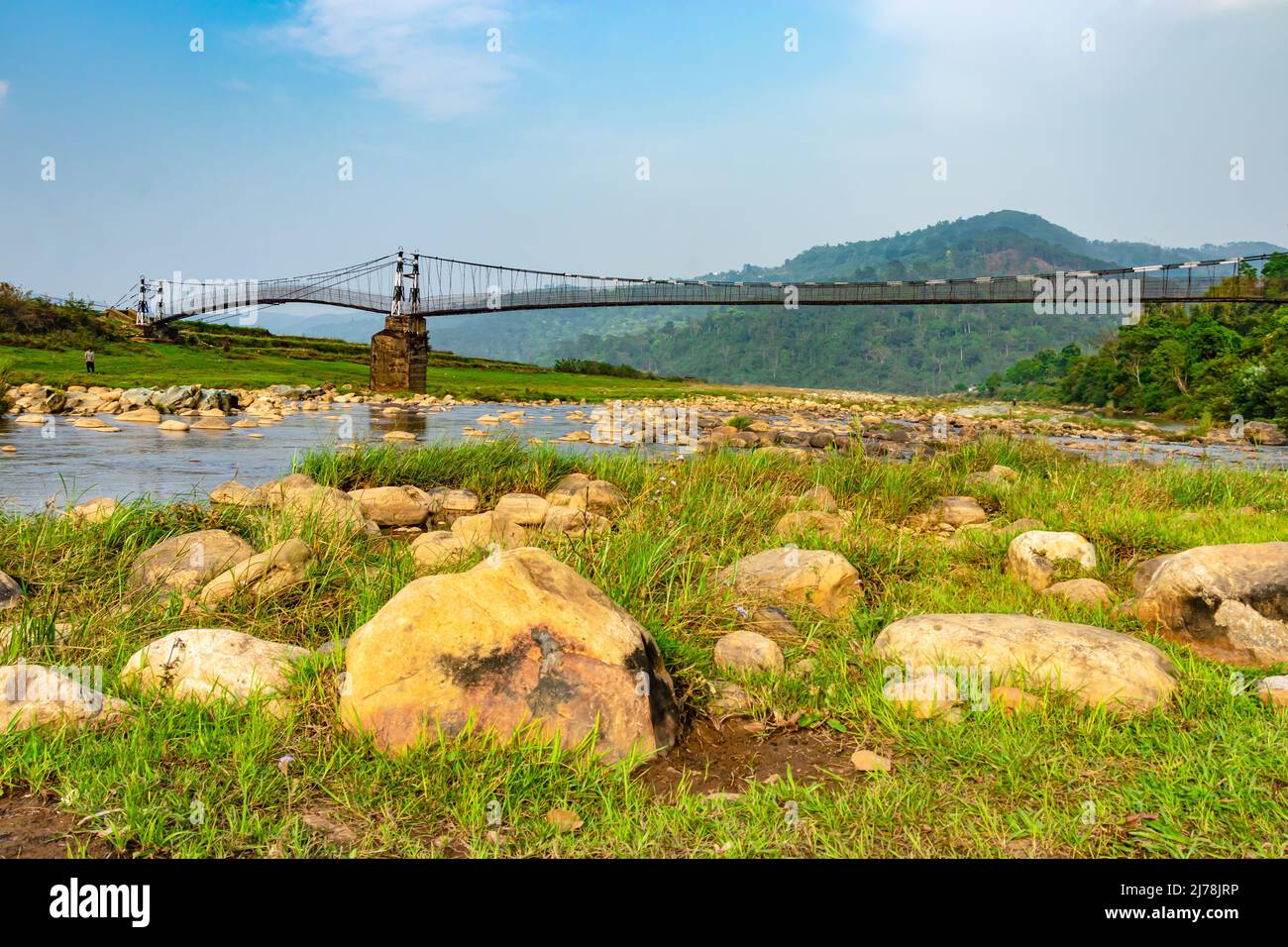 isolated iron suspension bridge over flowing river with mountain and ...