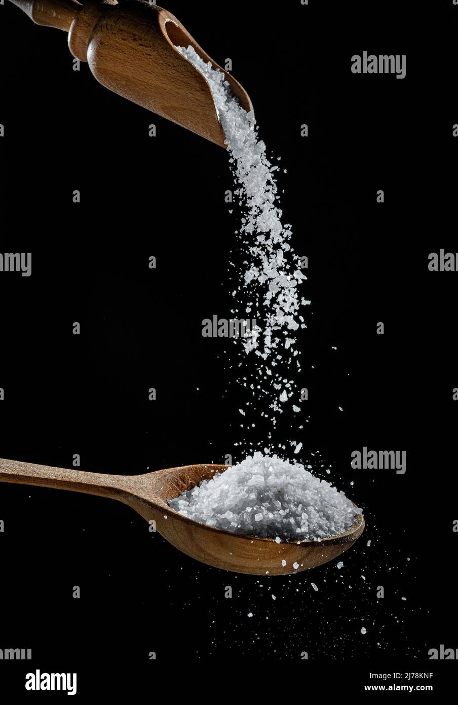 Edible salt crystals falling down into the wooden spoon at black ...