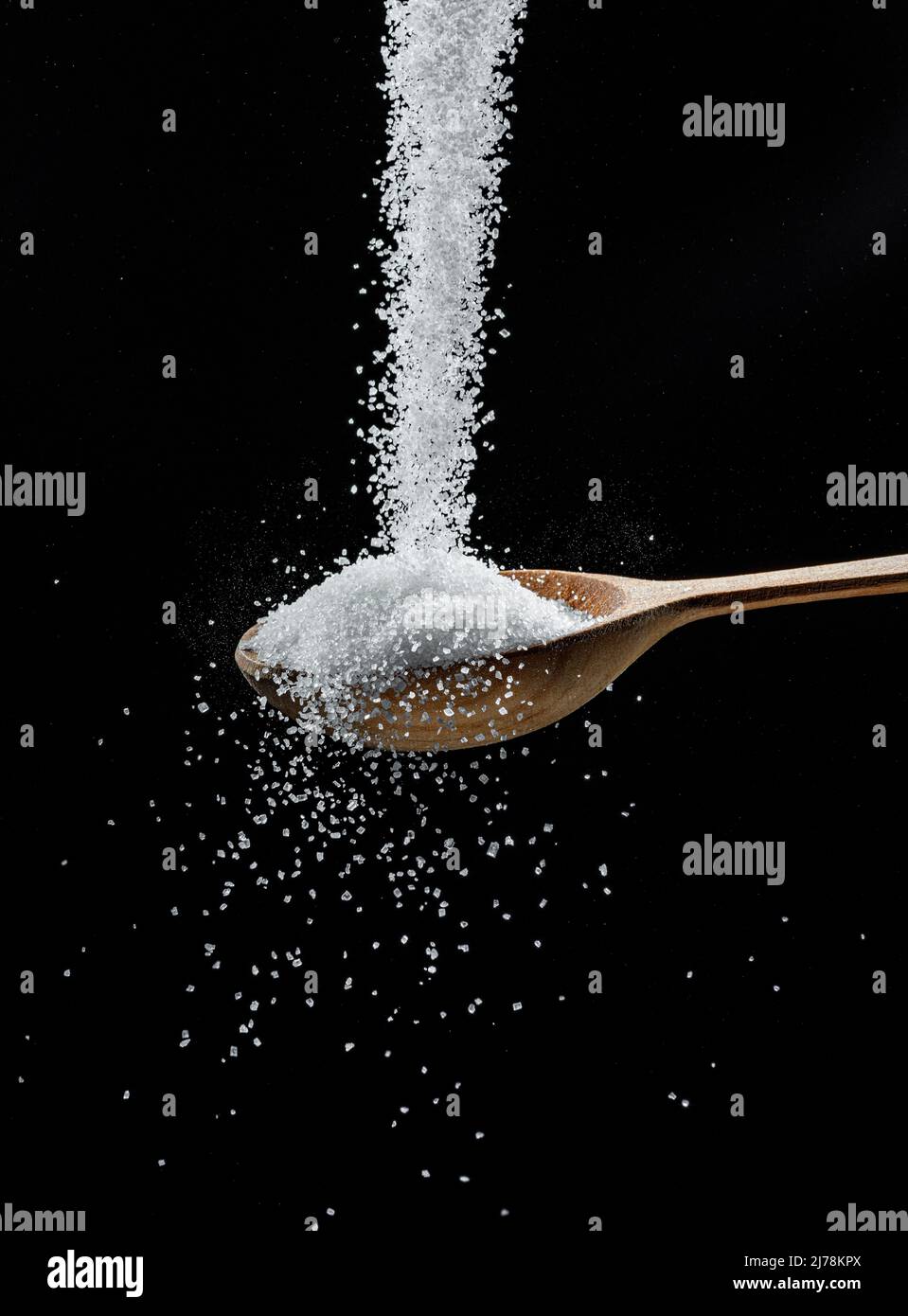 White refined sugar crystals falling down into the wooden spoon at ...
