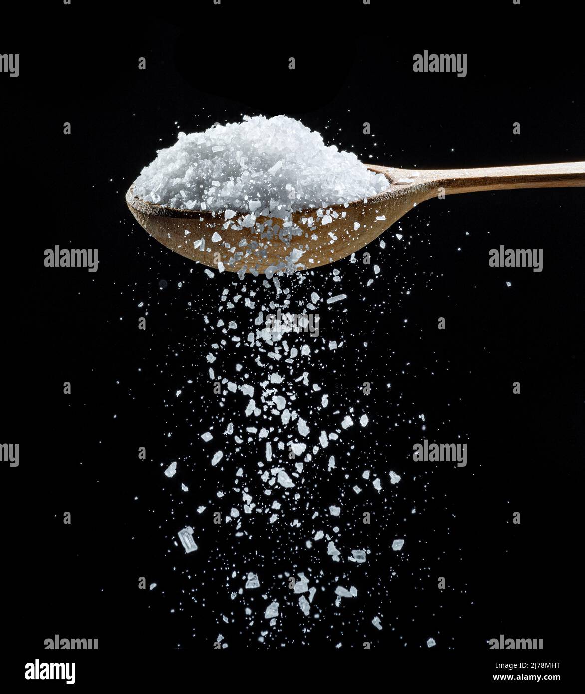 Edible salt crystals falling down into the wooden spoon at black ...