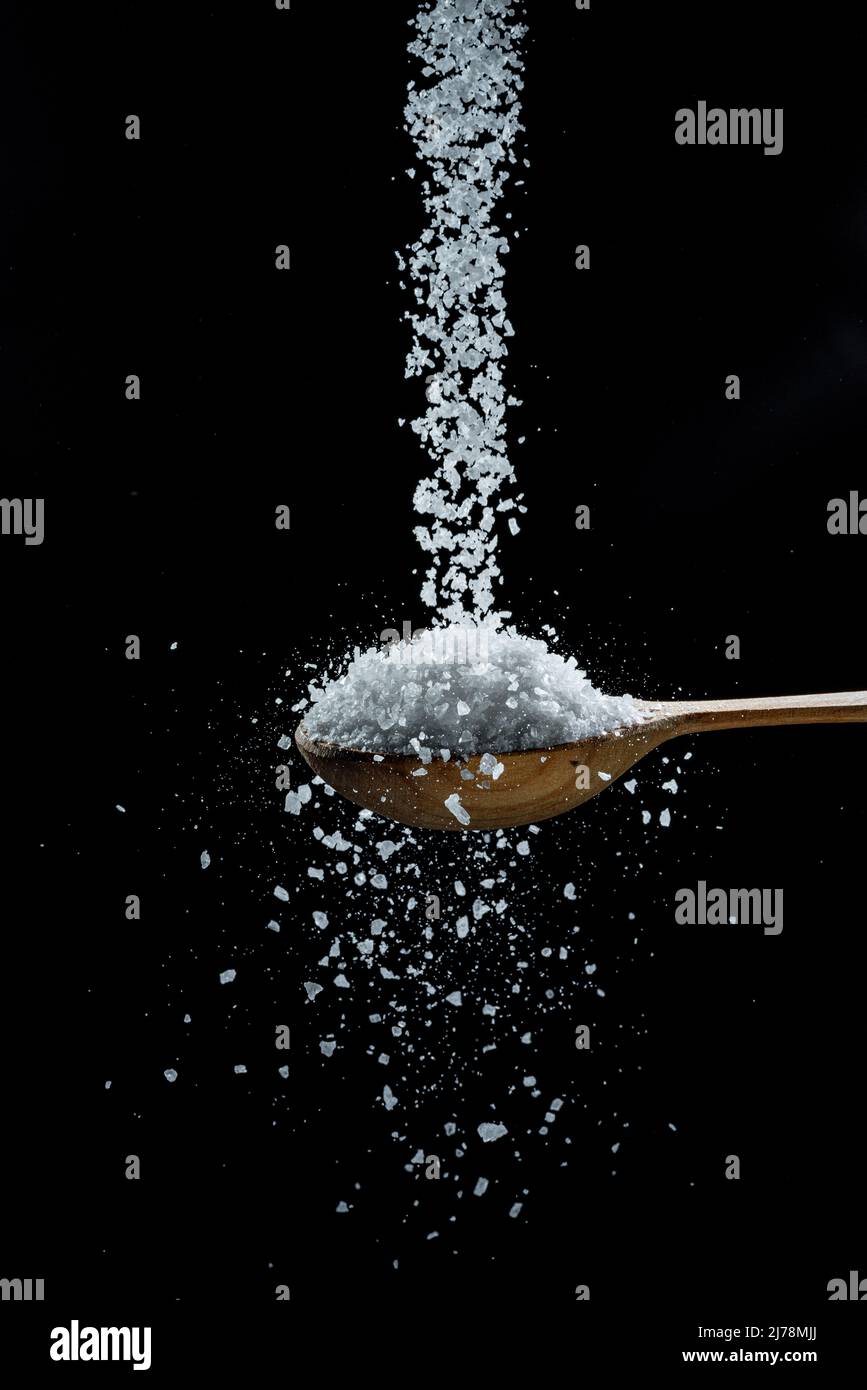 Edible salt crystals falling down into the wooden spoon at black ...