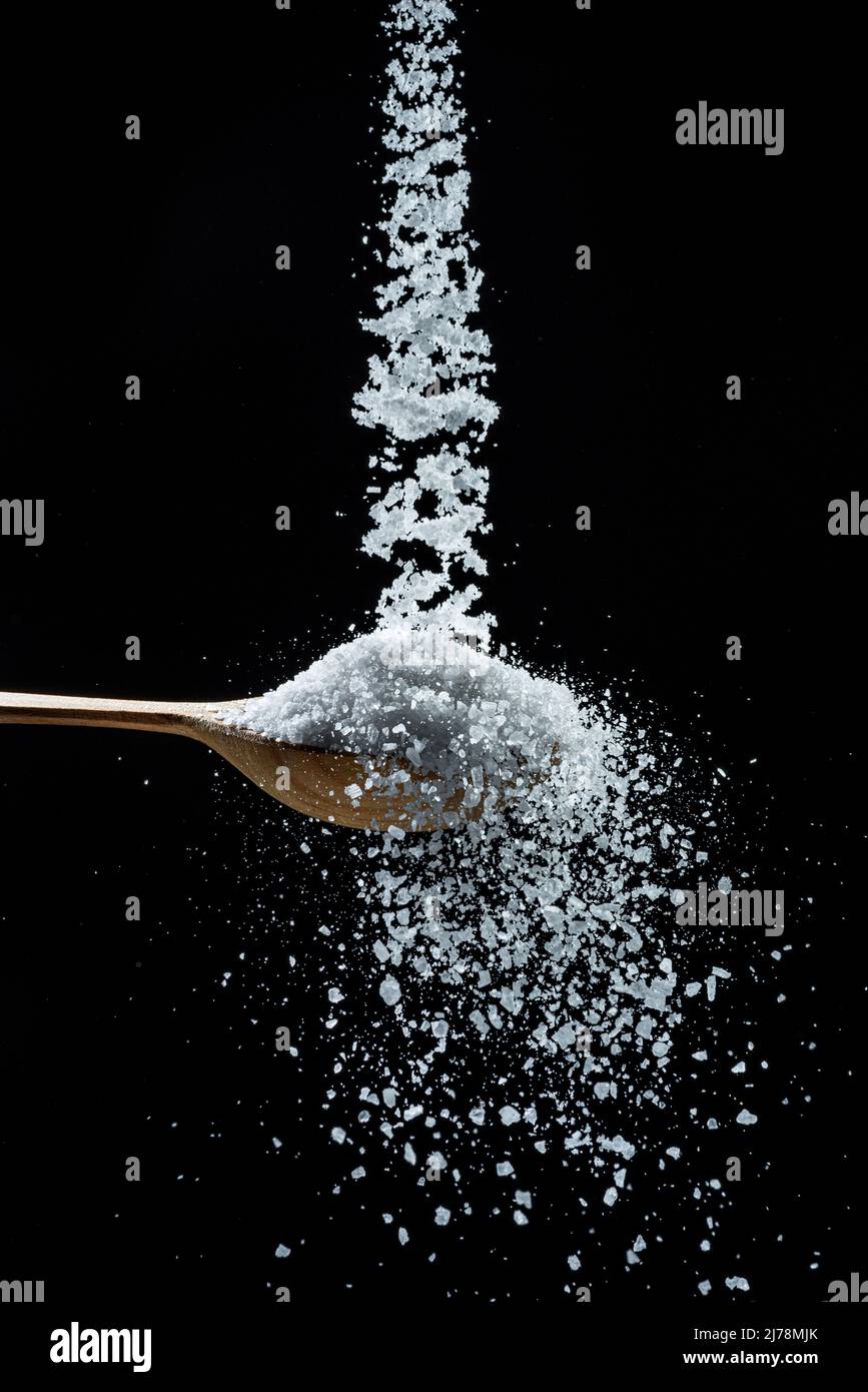 Edible salt crystals falling down into the wooden spoon at black ...