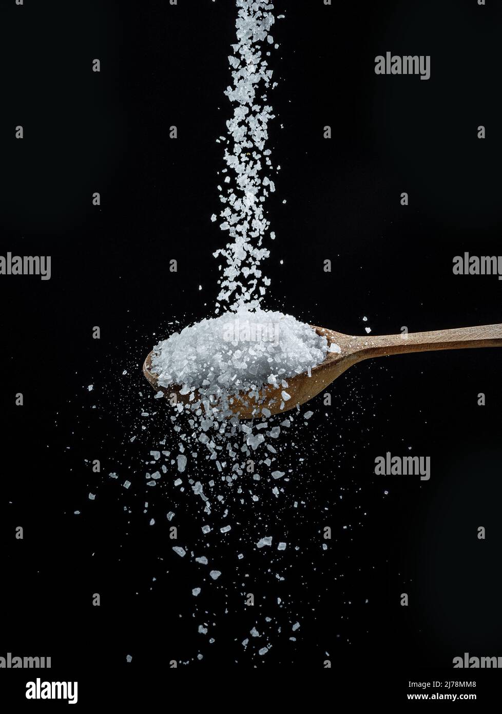 Edible salt crystals falling down into the wooden spoon at black ...