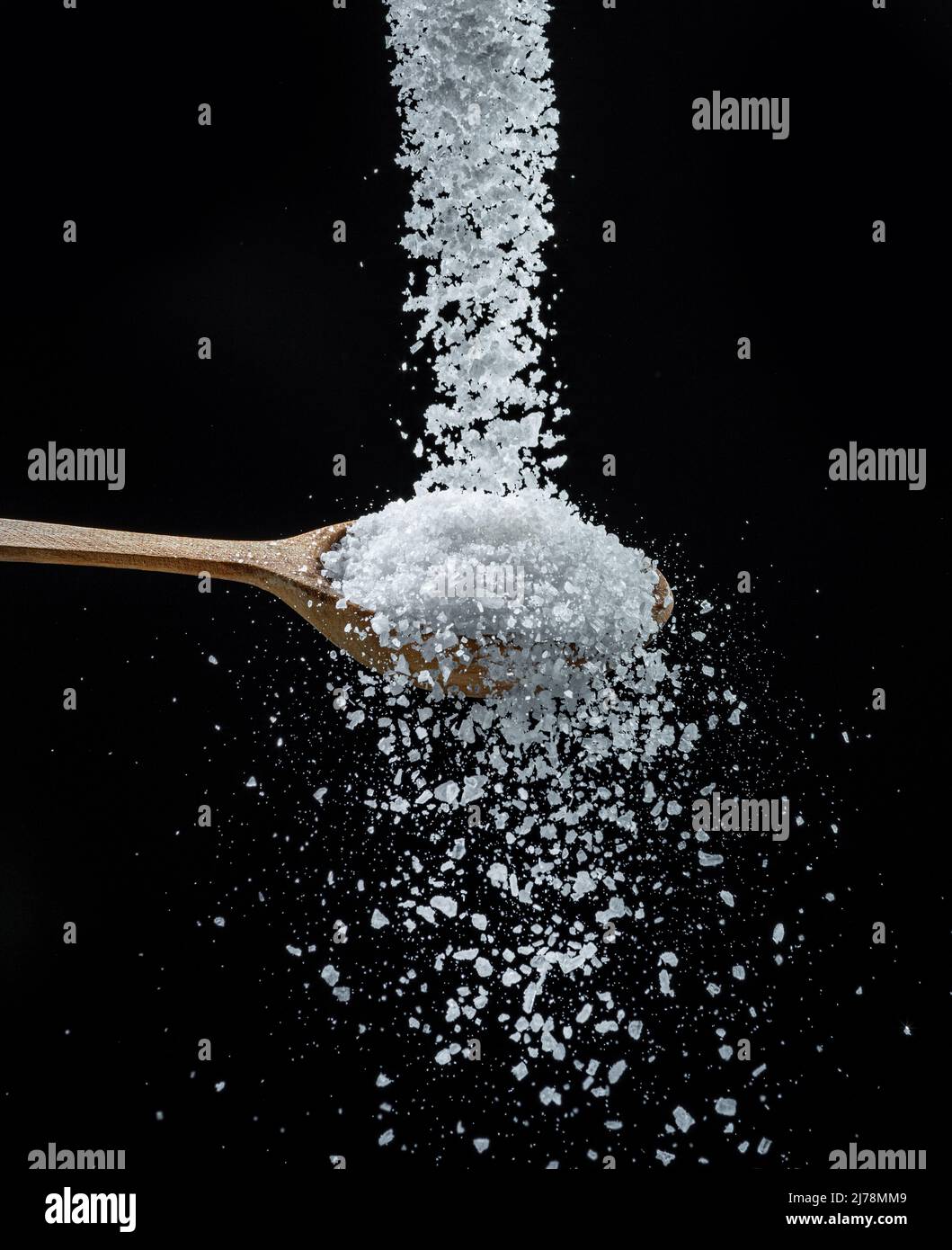 Edible salt crystals falling down into the wooden spoon at black ...