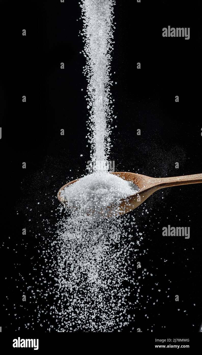 White refined sugar crystals falling down into the wooden spoon at ...