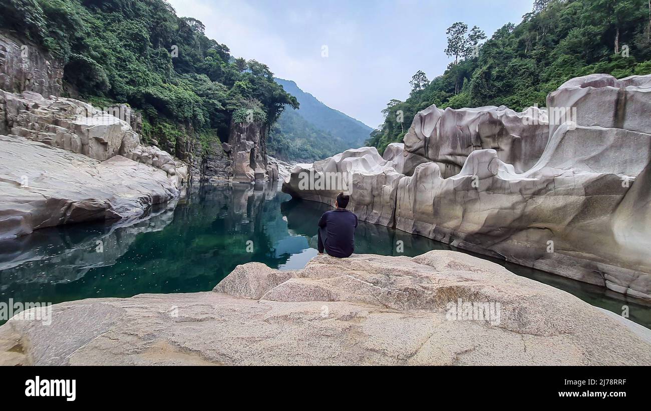 isolated young man sitting on naturally formed white shiny stone in ...