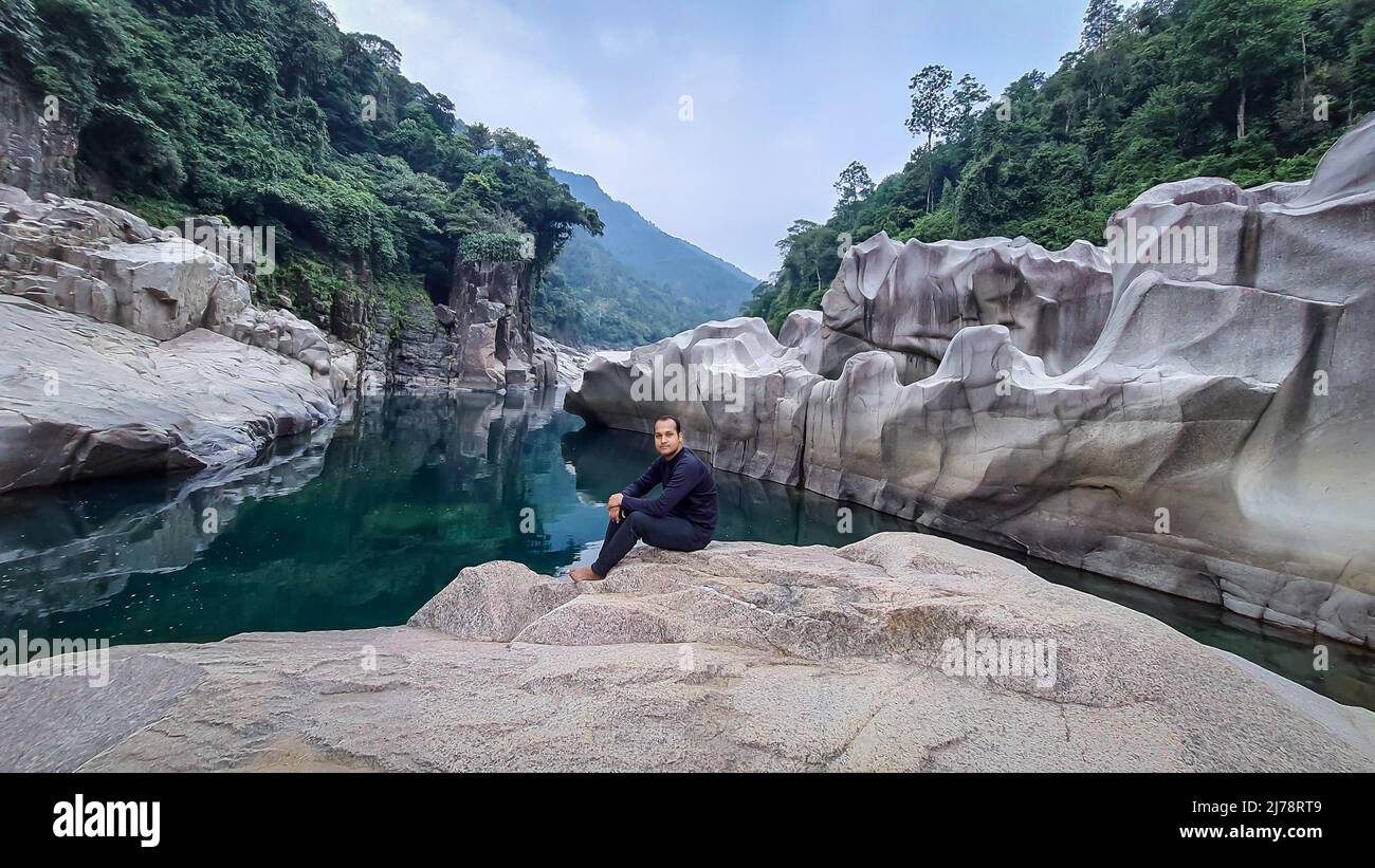 isolated young man sitting on naturally formed white shiny stone in ...