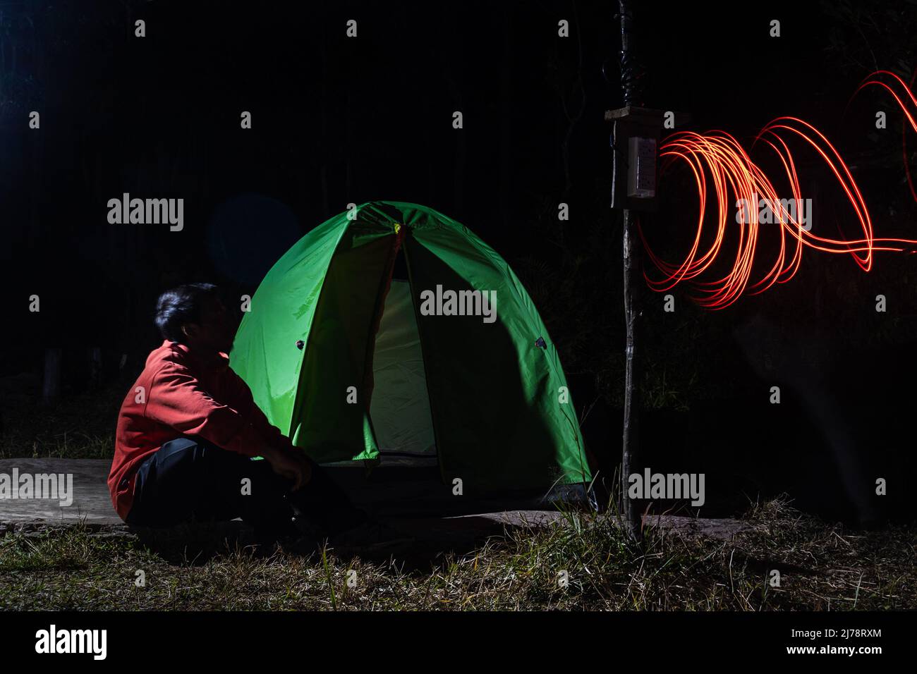 camping adventure at night with light trails and man sitting in ...