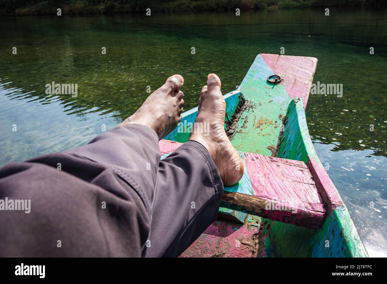 man foot resting on wood boat at river shore at morning from top angle ...