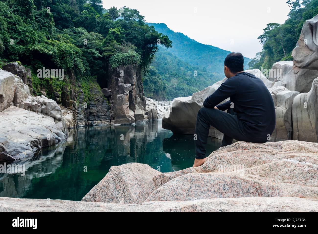 isolated young man sitting on naturally formed white shiny stone in ...