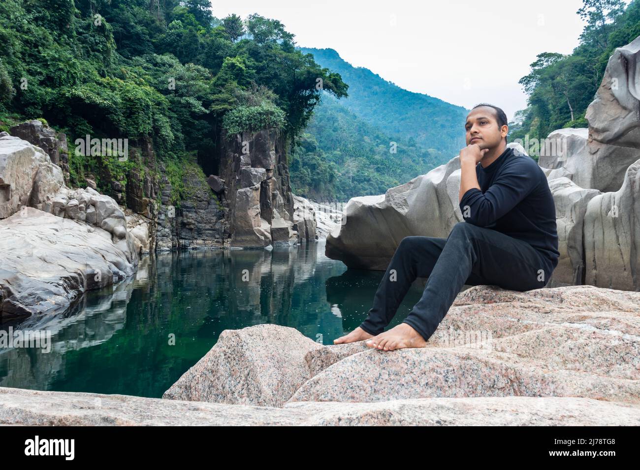 isolated young man sitting on naturally formed white shiny stone in ...