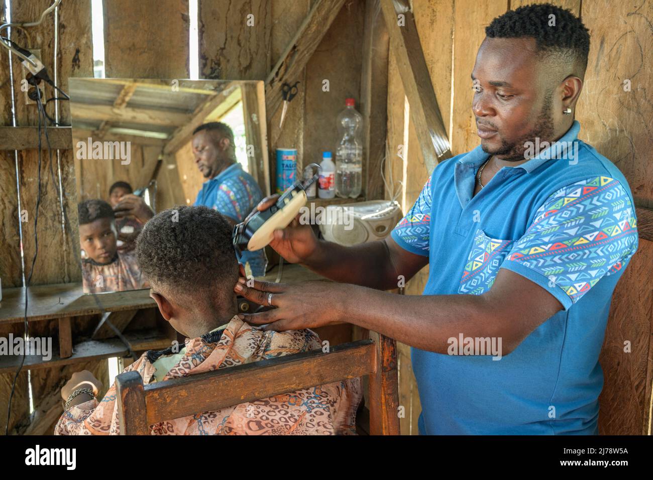 Barber cutting a boy's hair with a shaving machine in a humble street ...