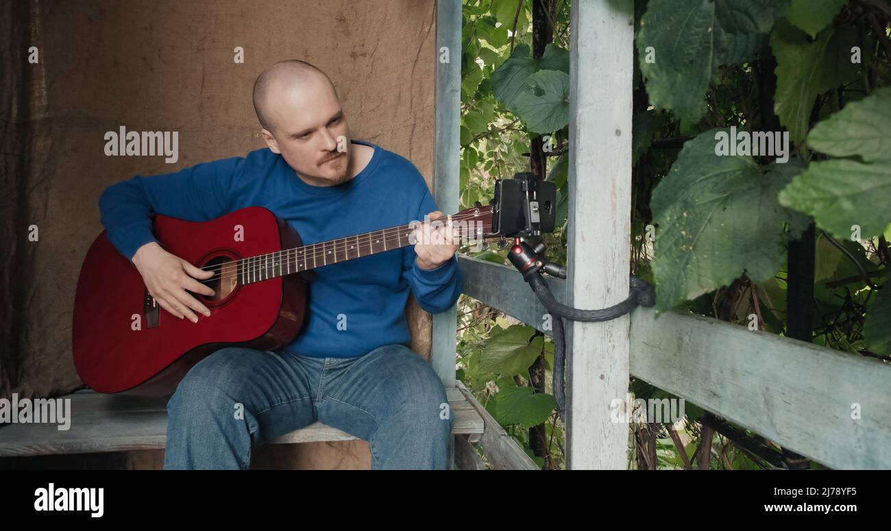 Man leads an online acoustic guitar lesson from the porch of his ...