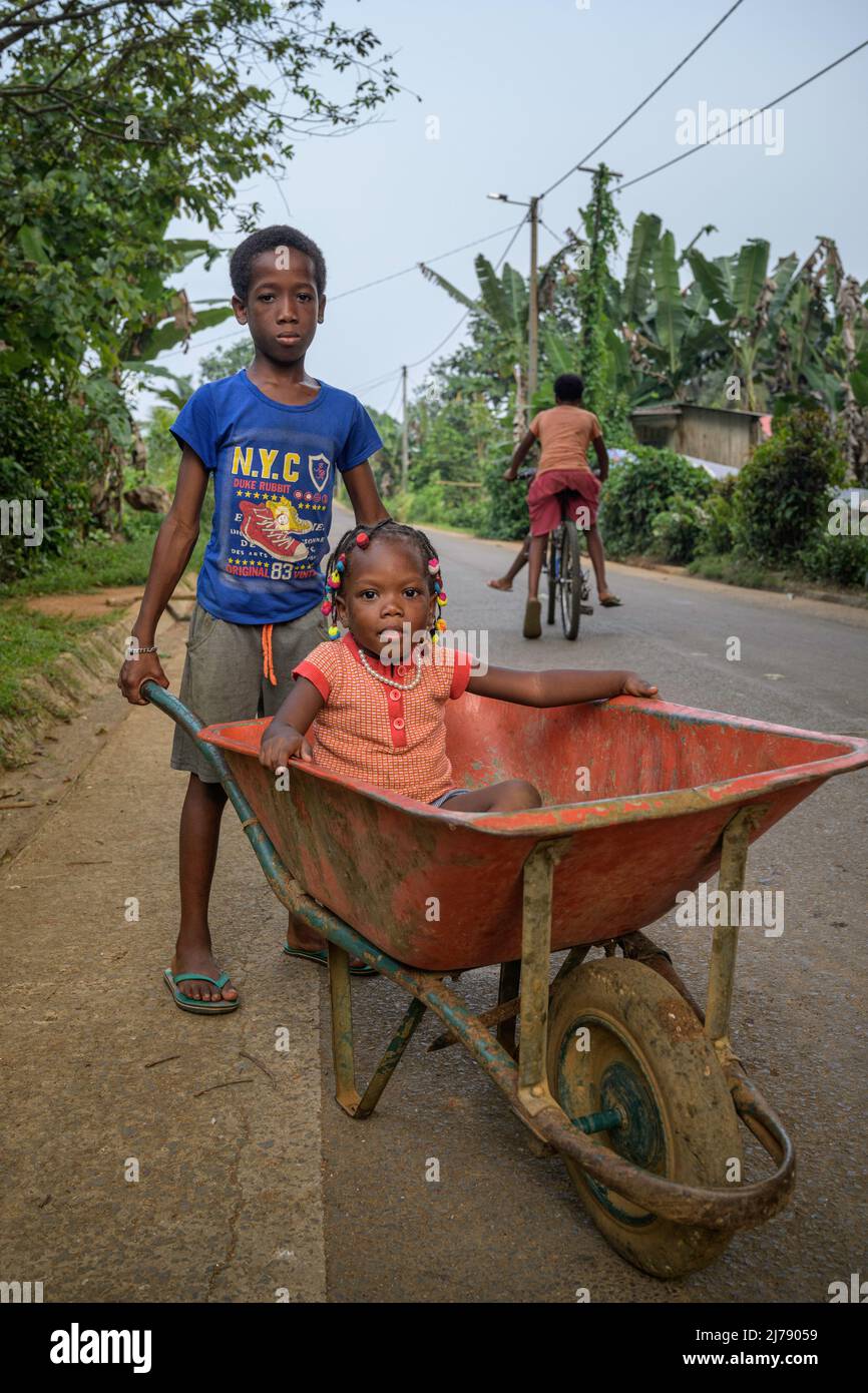 Children playing with a wheelbarrow by the road in the village of Picao ...