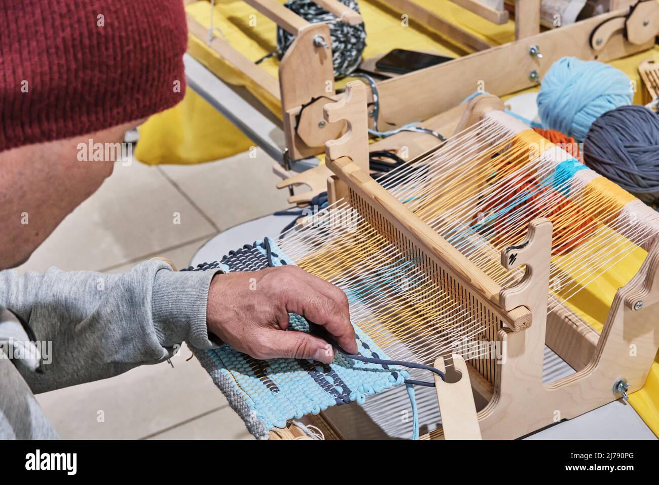 Hand of older man, who weaving small rug with pattern on wooden manual ...