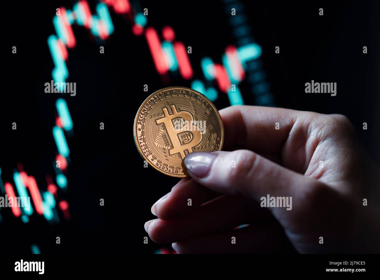 Hand holding a gold Bitcoin cryptocurrency coin with candle stick graph ...