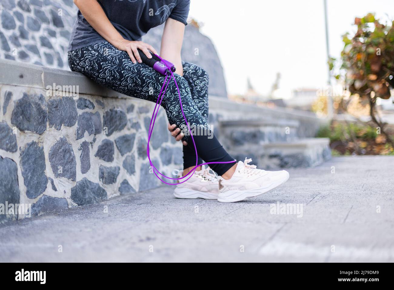 Young woman with a skipping rope. Muscle ache after jumping with a ...