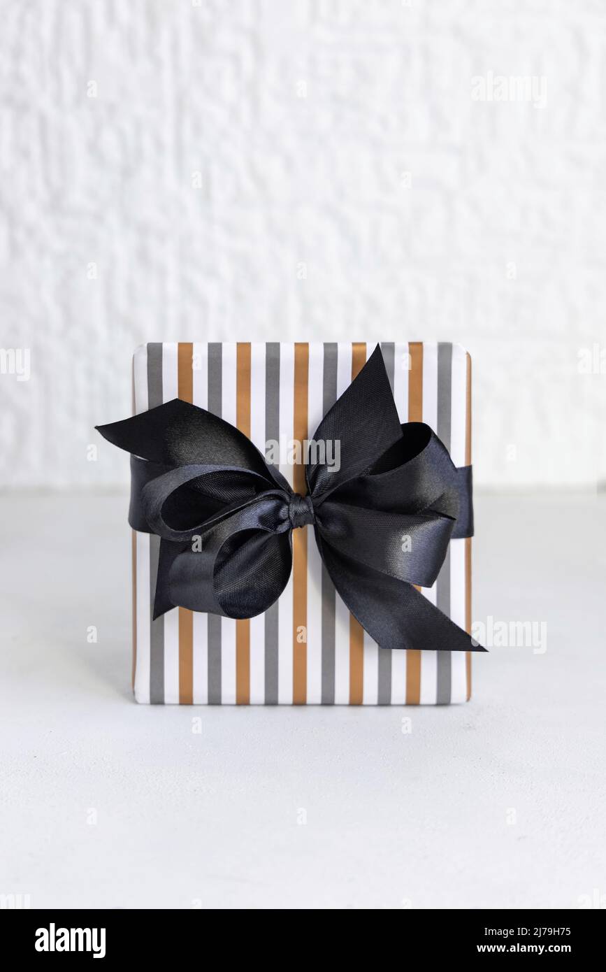 Gift box wrapped in Striped geometric paper with black ribbon bow close ...
