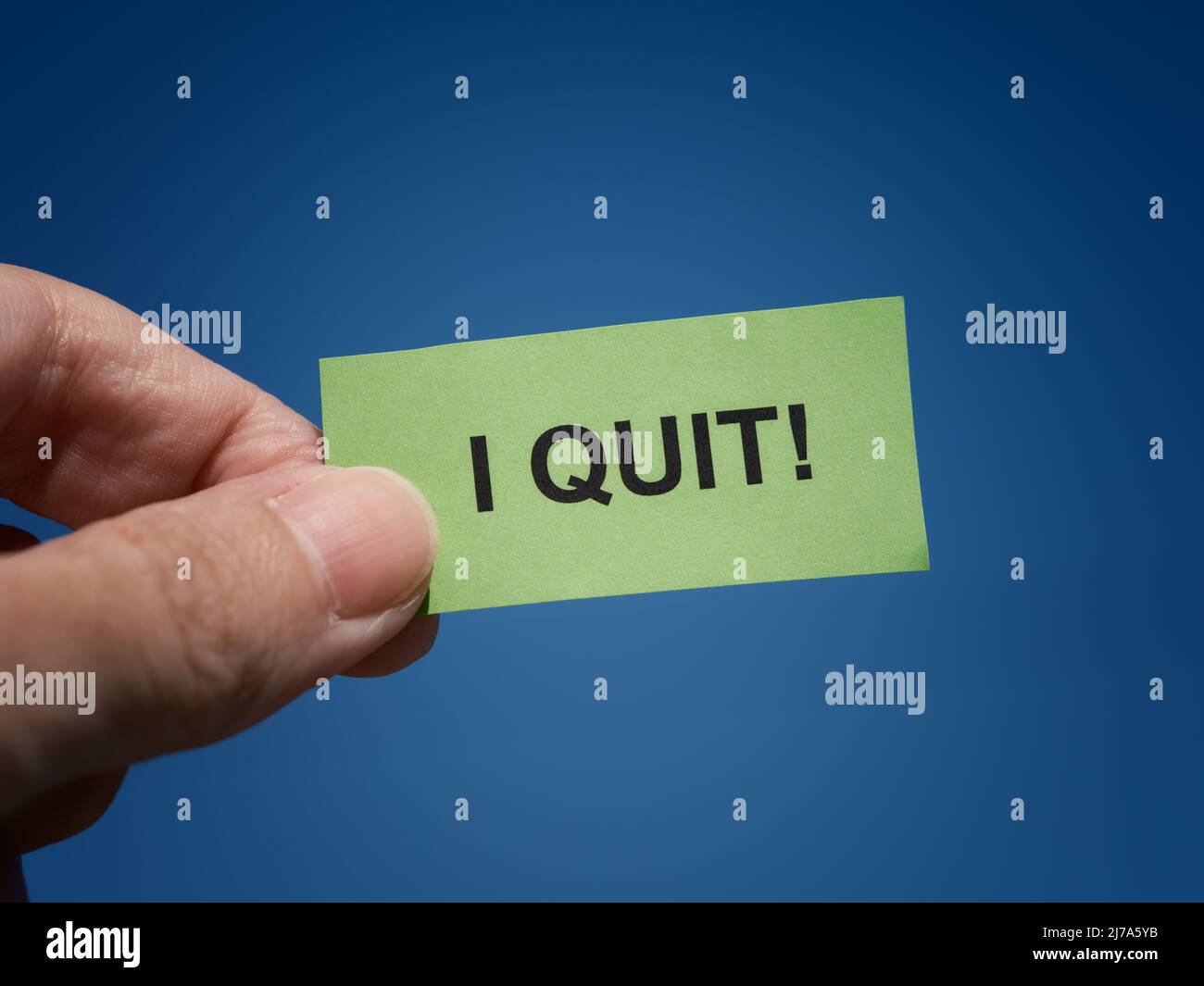 A man holding a green piece of paper with the words I Quit! on it in ...