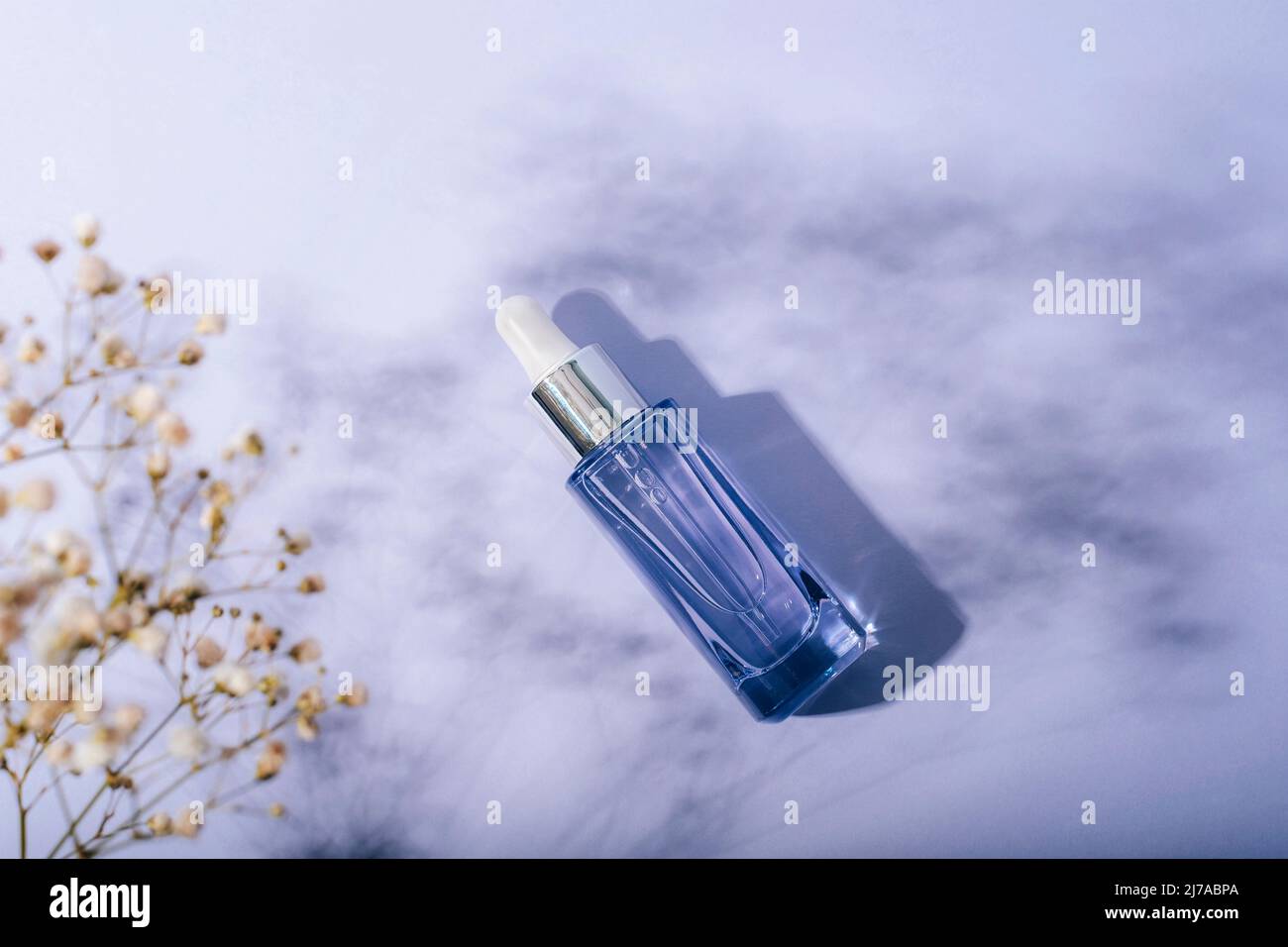 Purple serum bottle and gypsophilla flowers, hard shadows. Natural ...