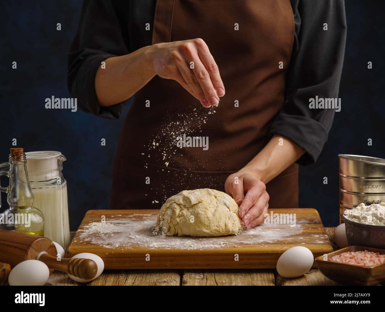 The chef sprinkles flour on the prepared dough on a wooden cutting ...