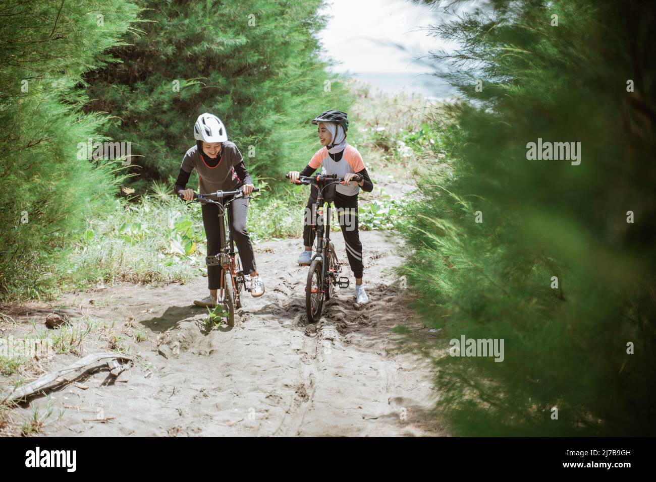 Two female cyclists pass a sandy road on a beach Stock Photo - Alamy
