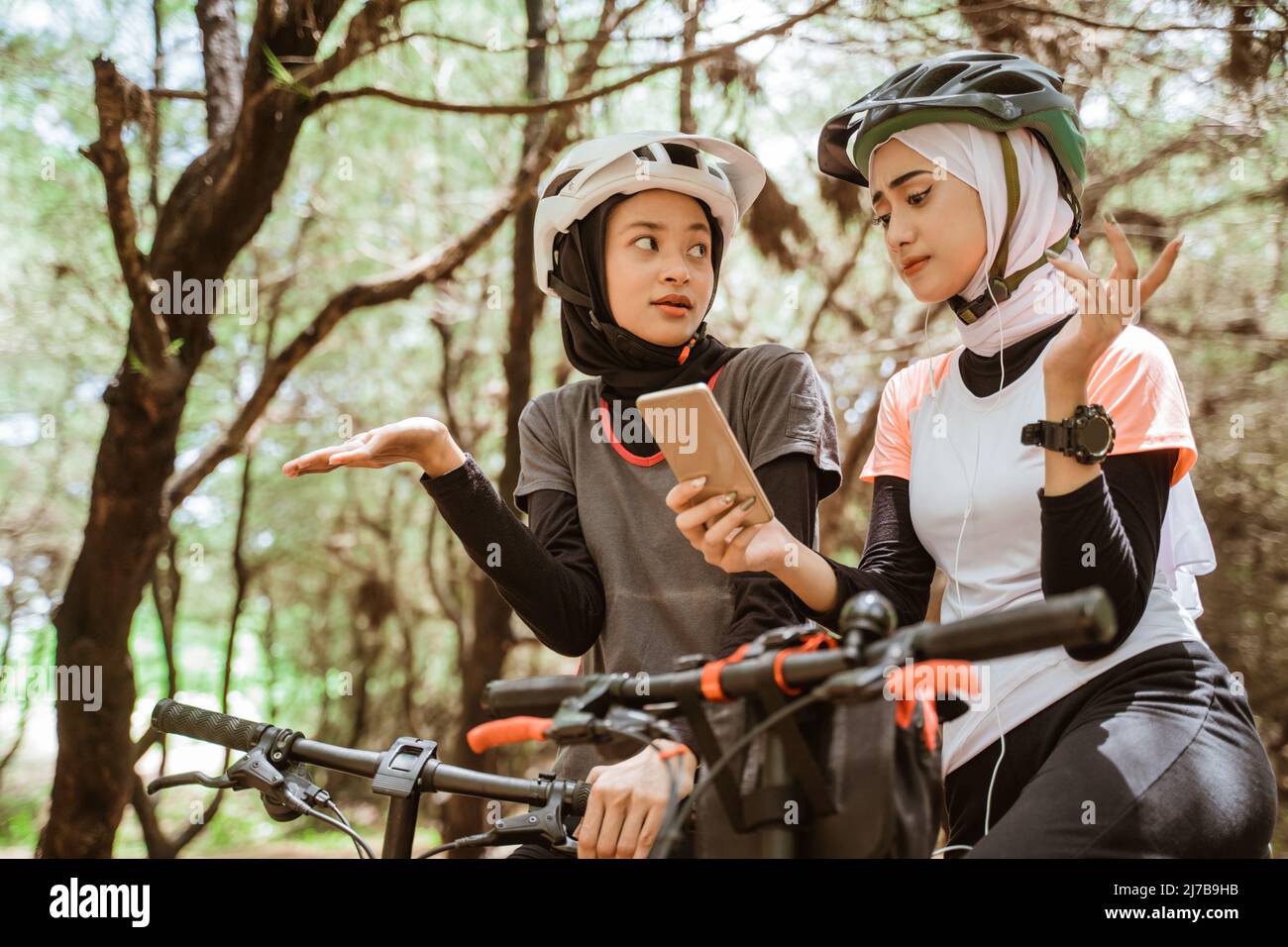 Two young women cycling with confused hand gestures Stock Photo - Alamy
