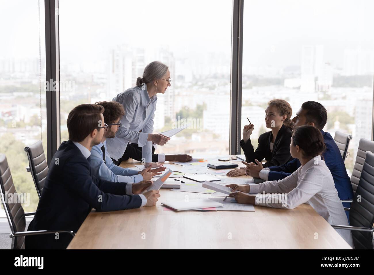 Mature grey haired female business mentor training group of interns ...