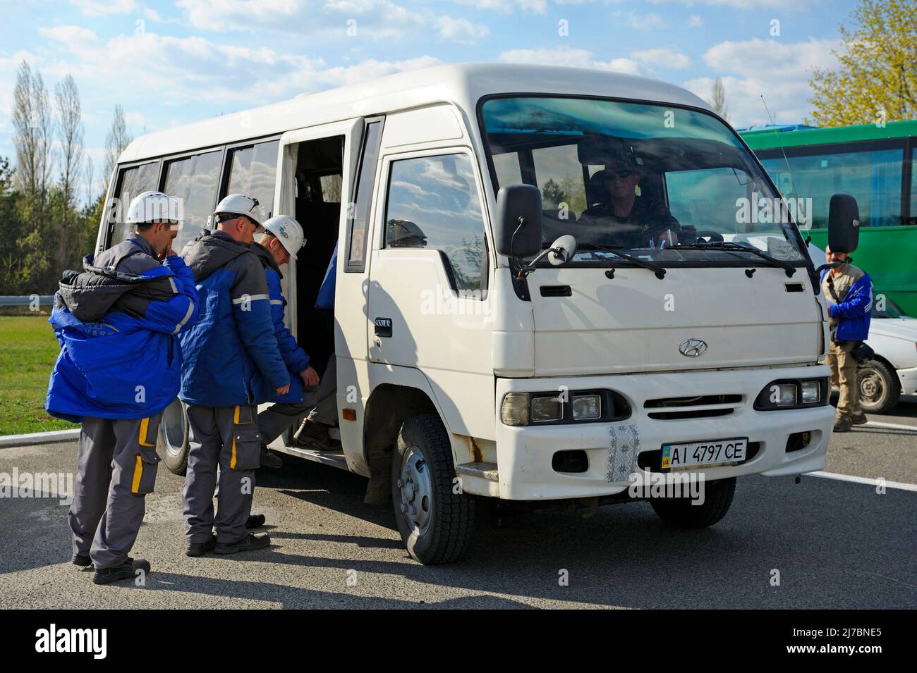 Workers in turnout coats get on the bus on the bus stop after day shift ...