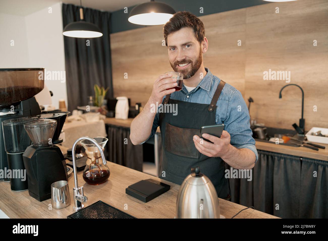 Handsome barista drinking coffee and scrolling through social media ...