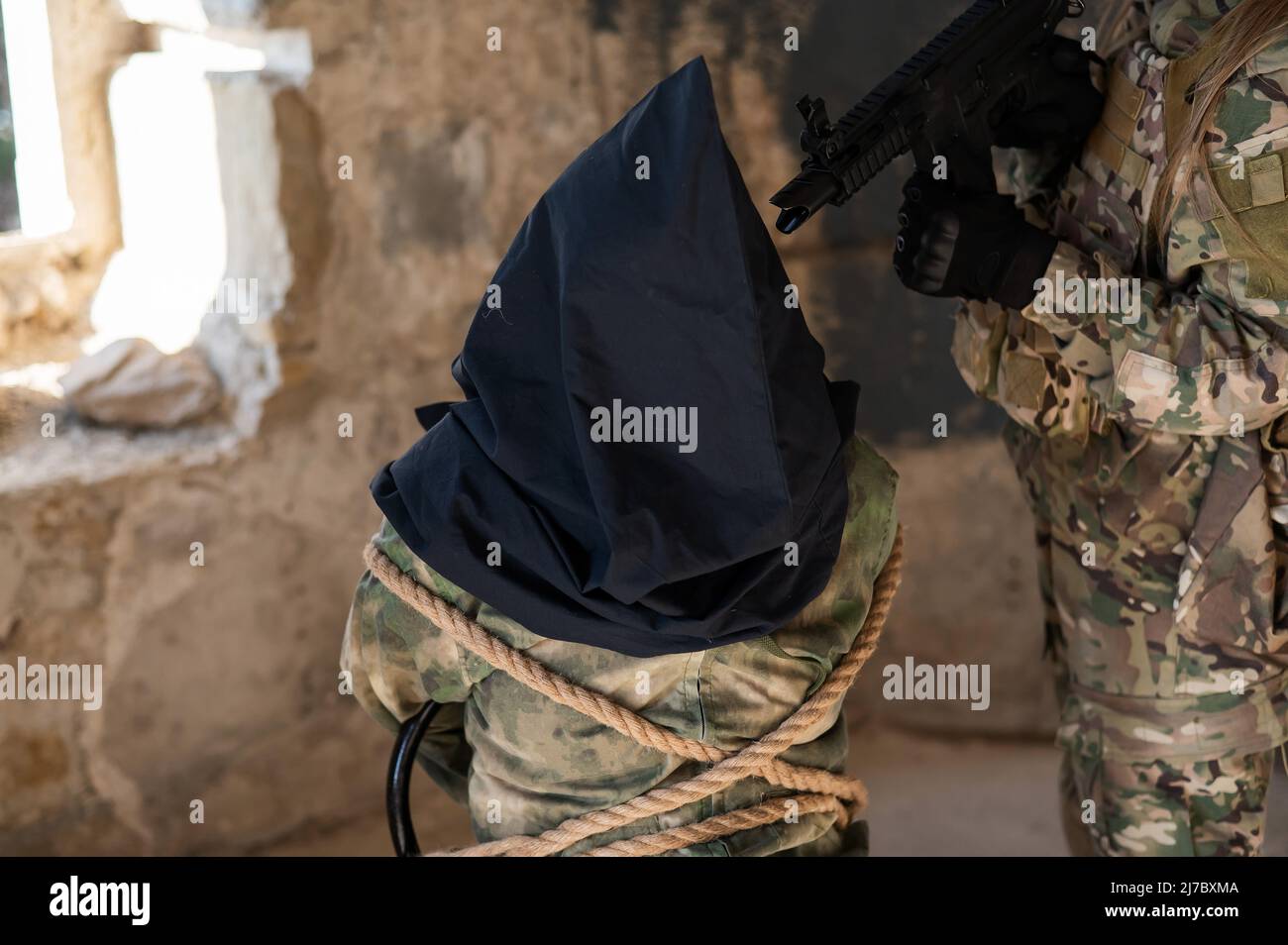 A caucasian woman in an army uniform holds a hostage with a bag on her ...