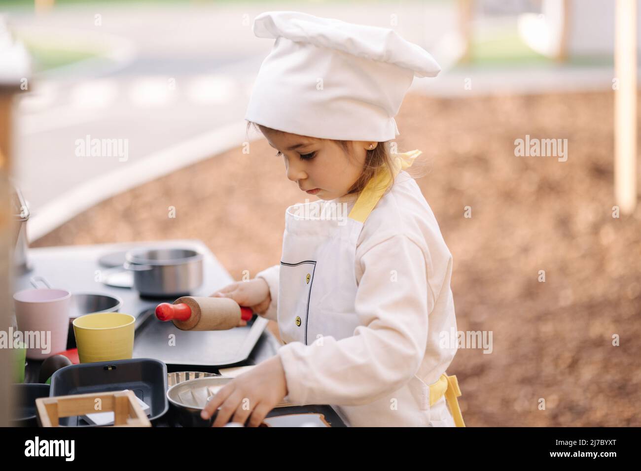 Adorable little girl in chef's coat and cap cooks at the children's toy ...