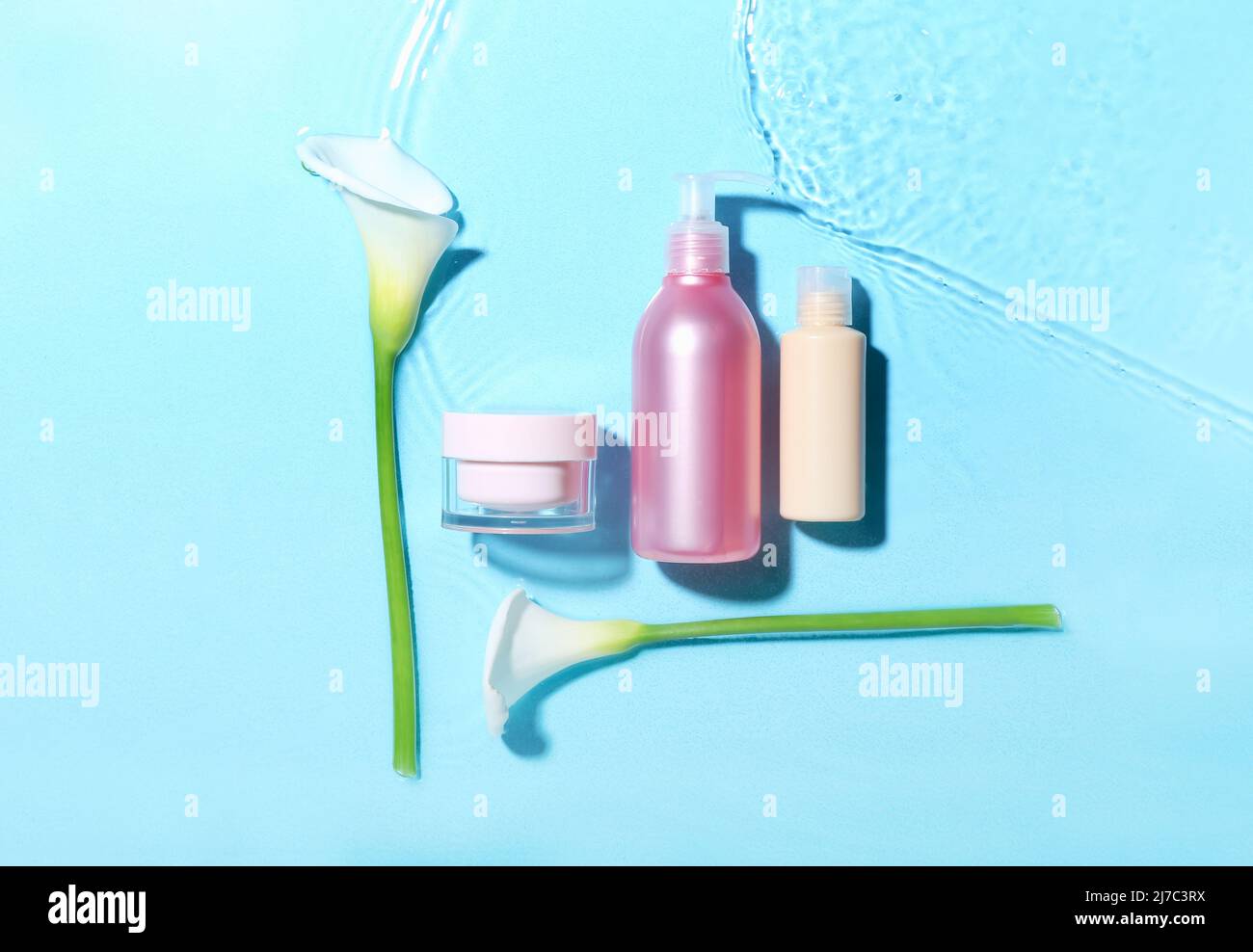 Different cosmetic products and calla lilies in water on blue ...