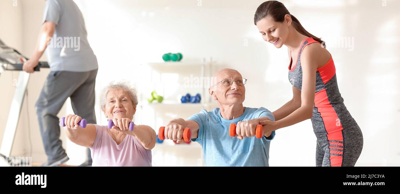 Young trainer helping elderly people to do exercises in gym Stock Photo ...