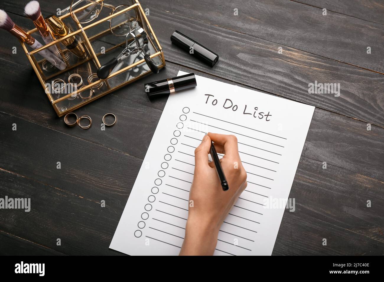 Female hand with to-do list, cosmetics and accessories on dark wooden ...