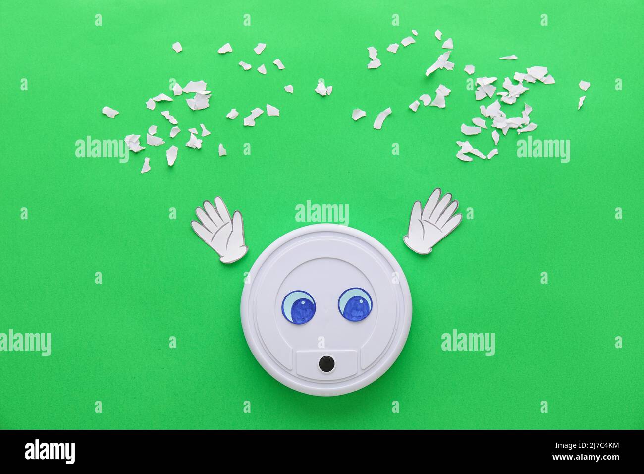 Modern robot vacuum cleaner with drawn eyes and paper pieces on green ...