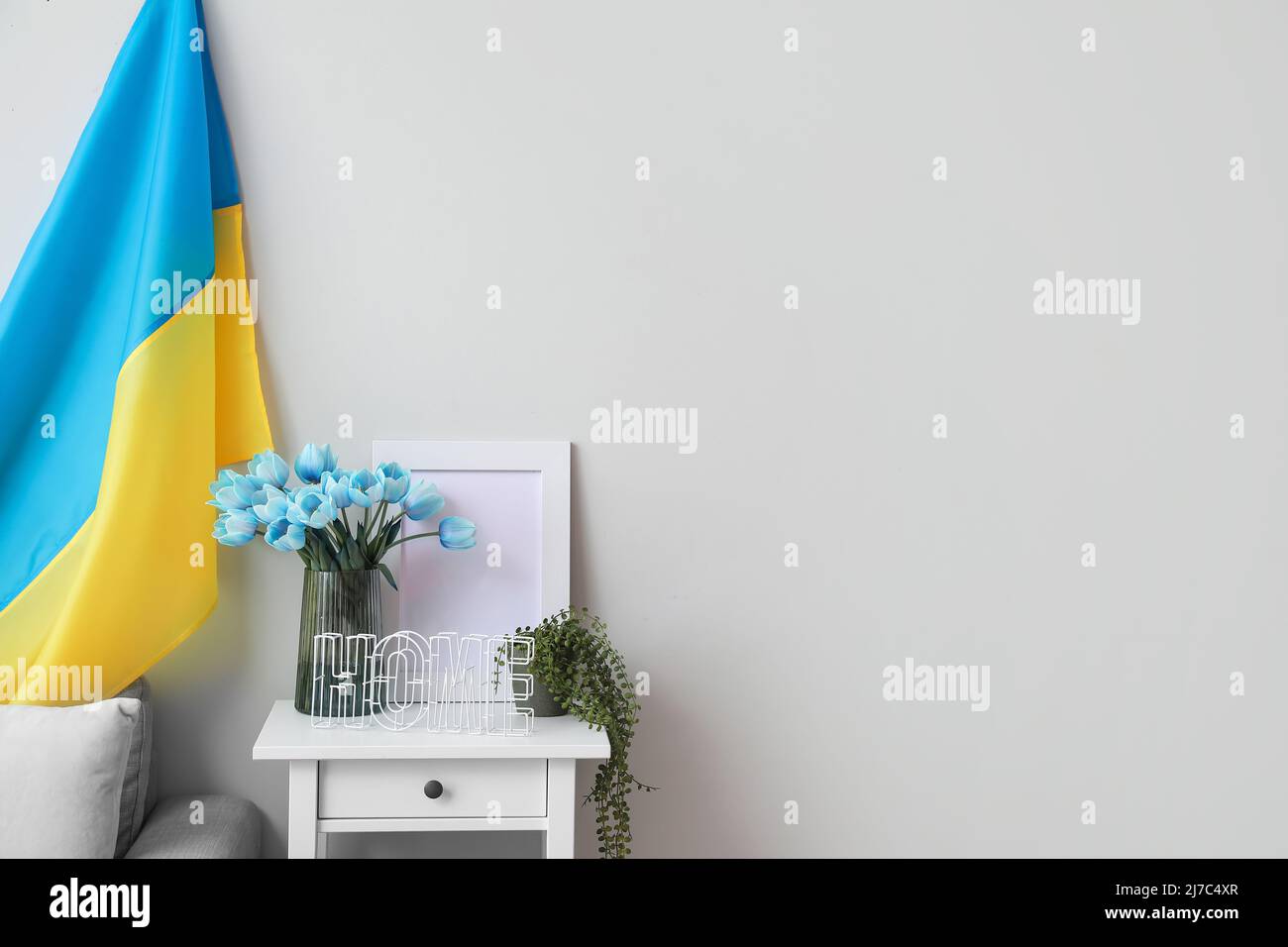Vase with tulips, flag of Ukraine, decor, frame and houseplant on table ...