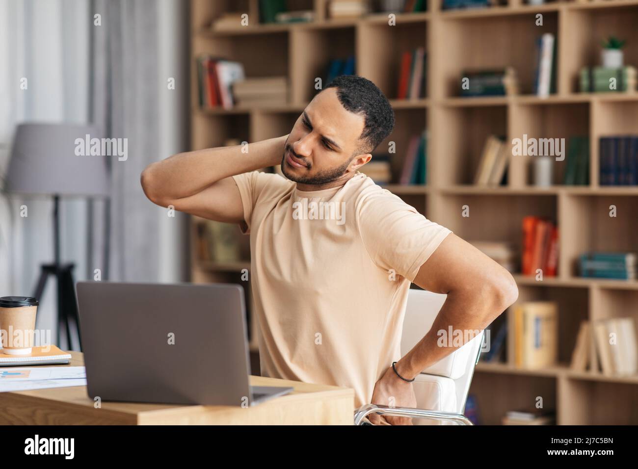 Young freelancer man touching aching neck and back, working on laptop ...