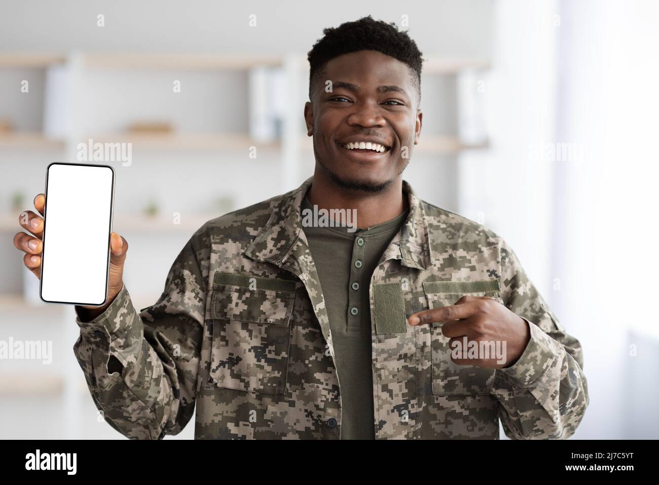 Happy black soldier in military uniform showing his smartphone, mockup ...