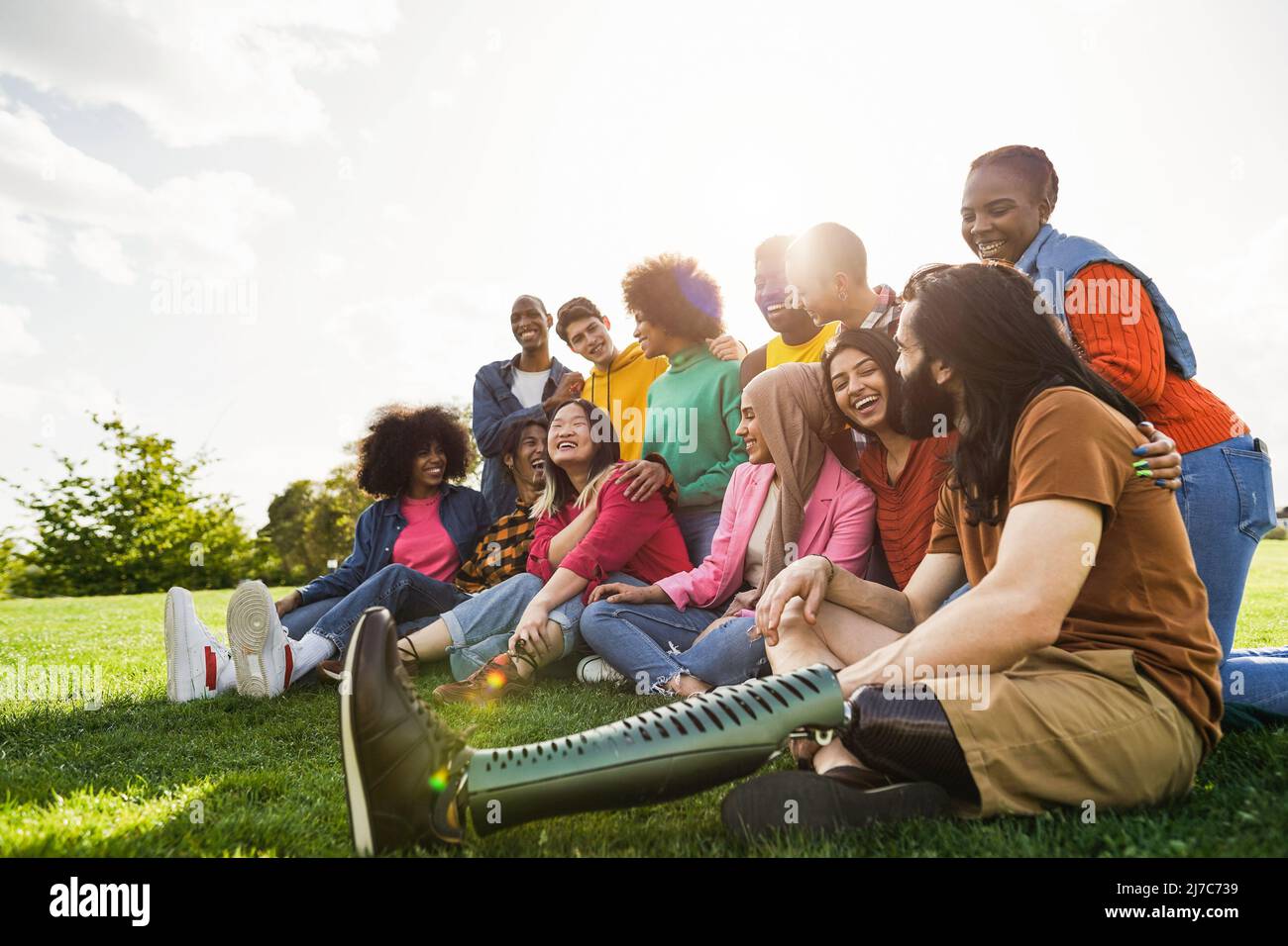 Multiethnic diverse people having fun outdoor sitting on grass at city ...