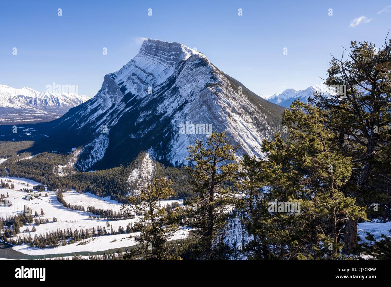 Snowcapped Mount Rundle mountain range with snowy forest over blue sky ...
