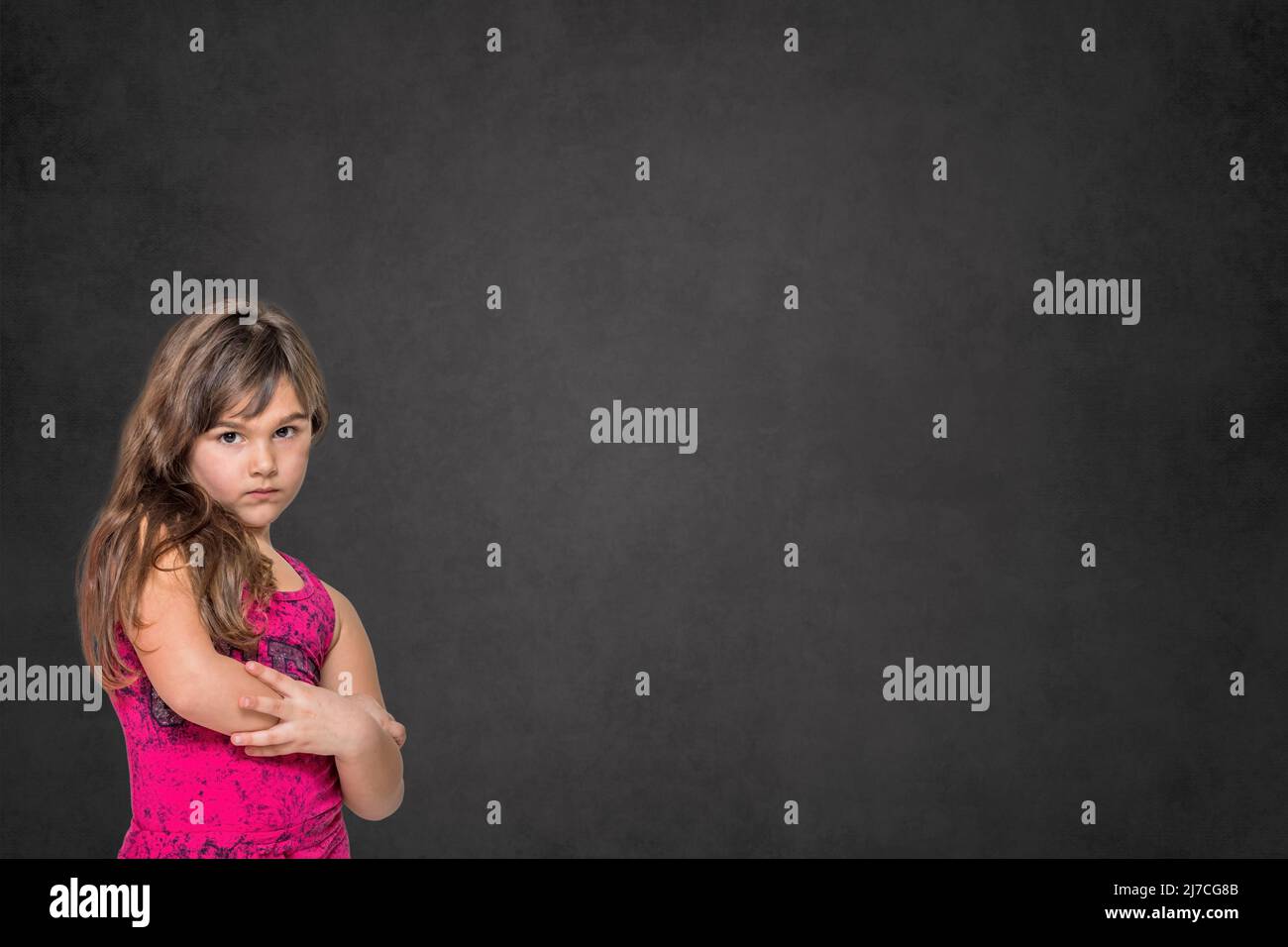 Serious long haired little girl is posing on the dark background ...