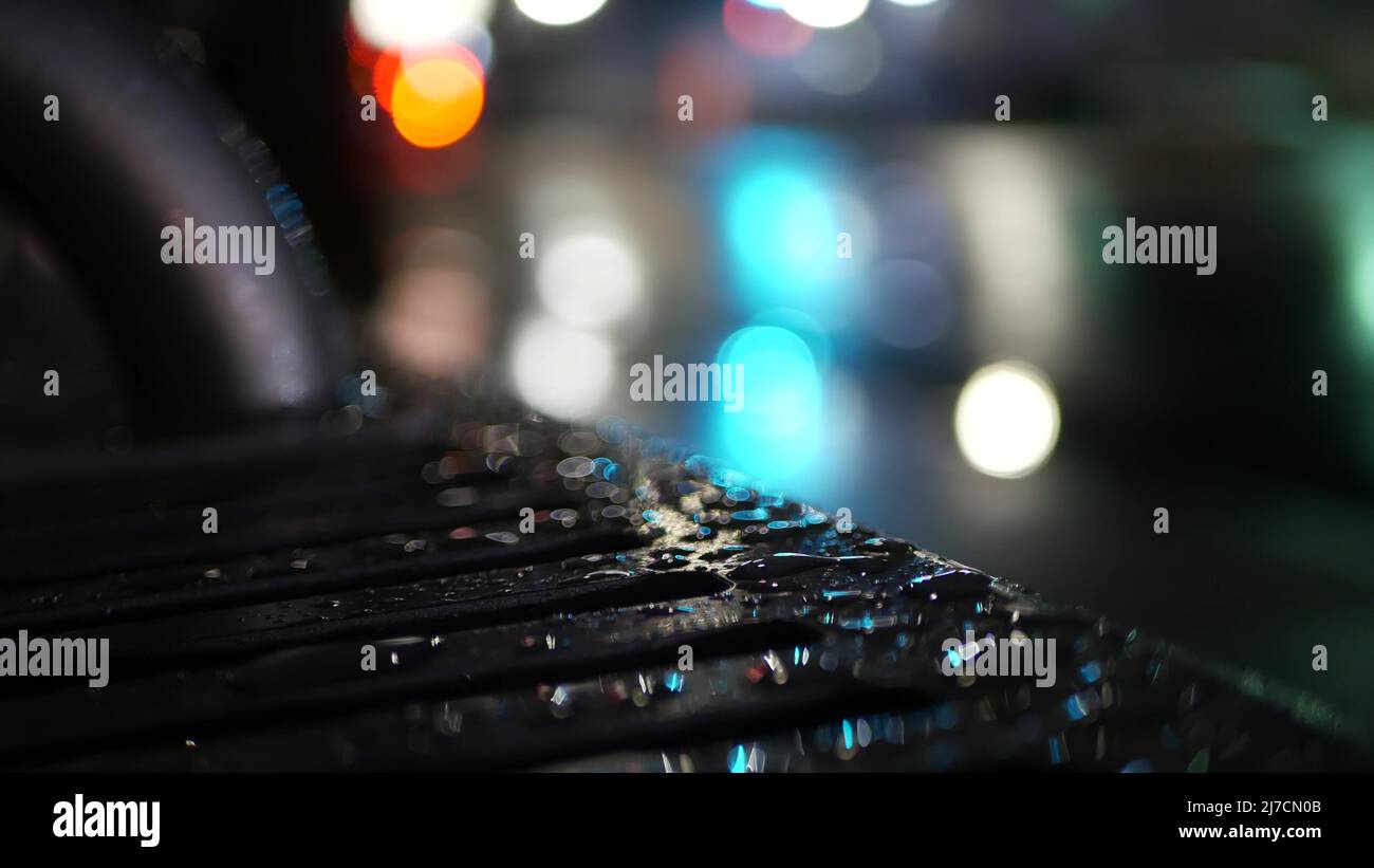 Car traffic lights bokeh, reflection on bus stop bench in rainy weather ...