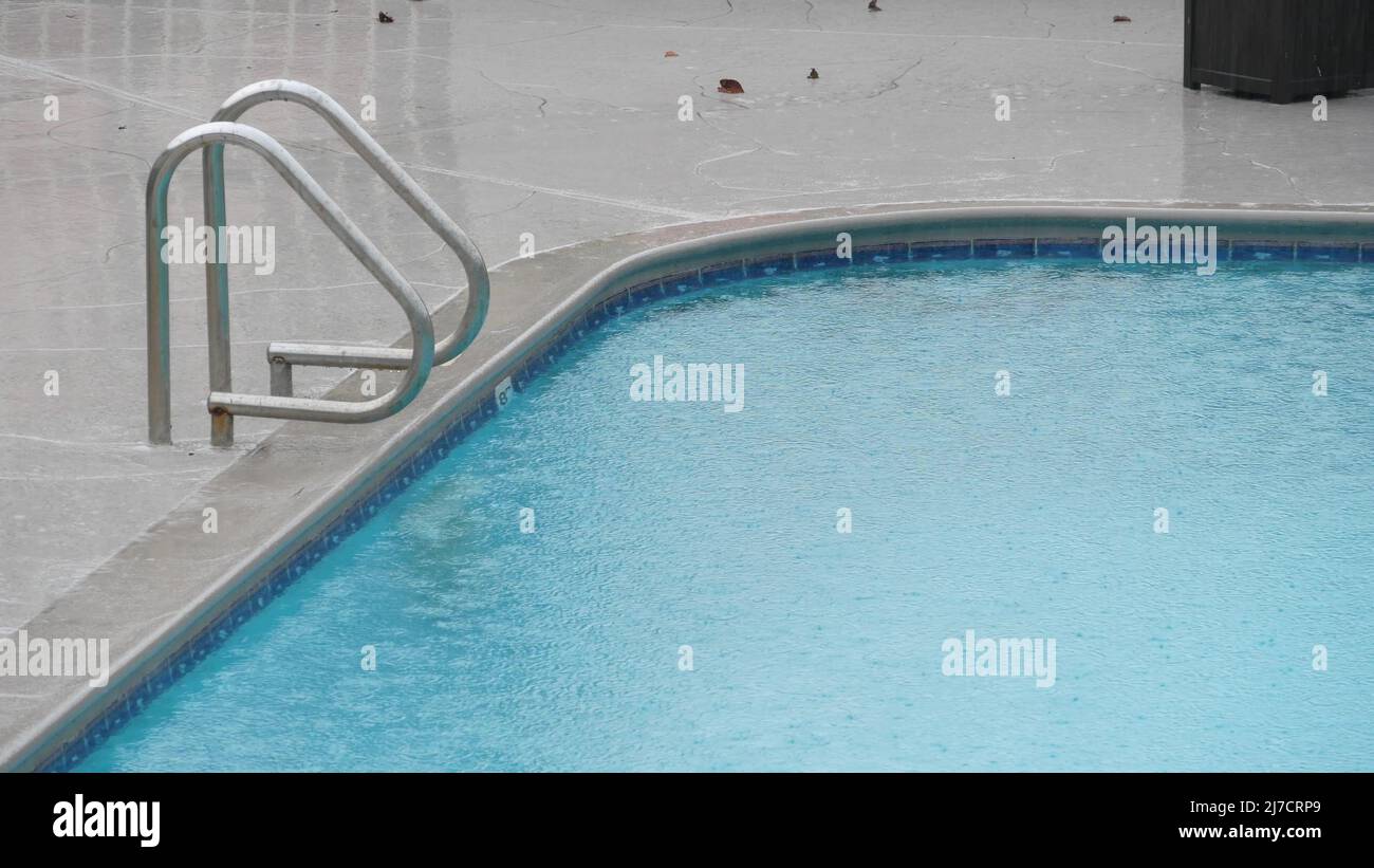 Rain drops falling on water surface of blue swimming pool, rainy day in ...