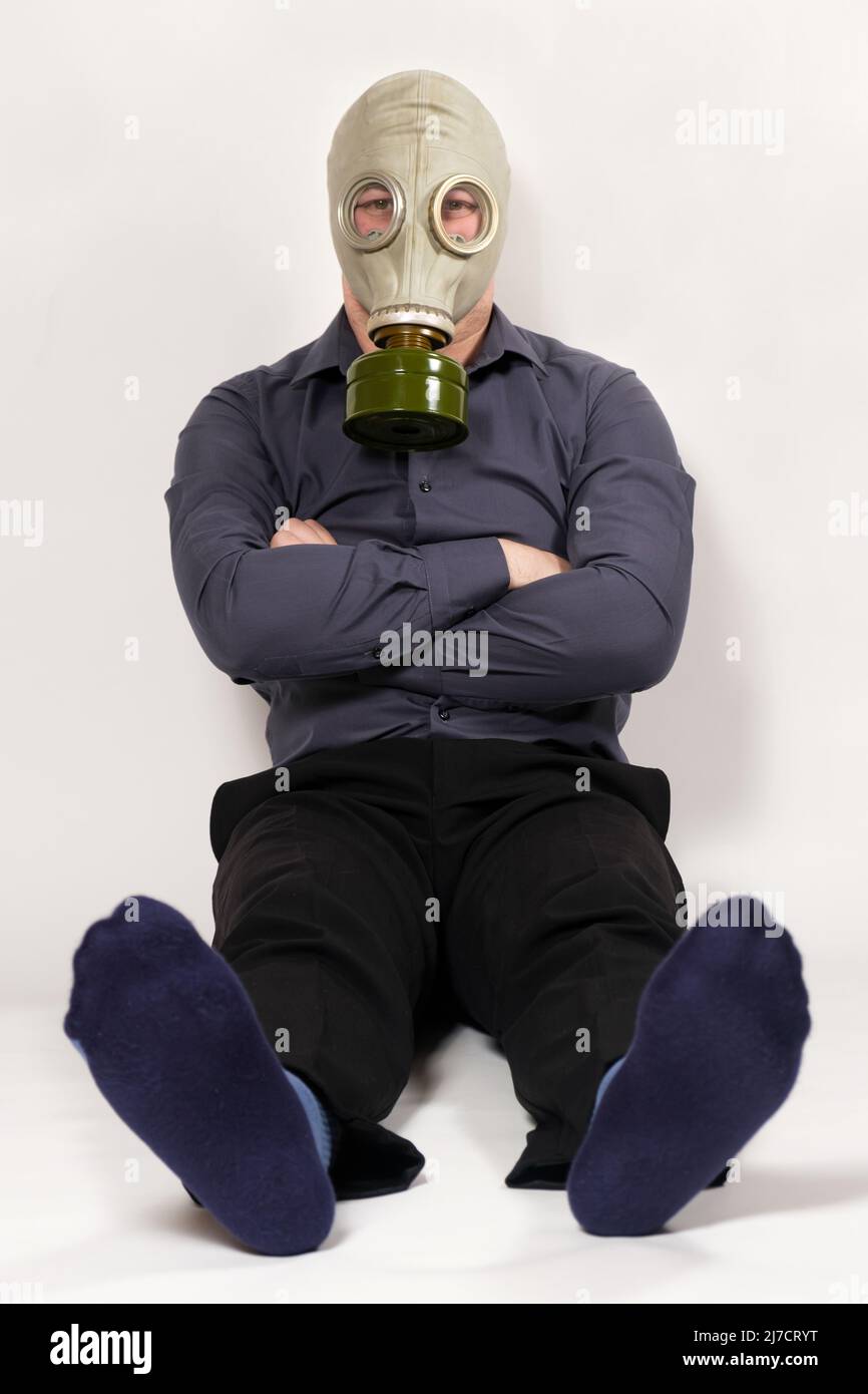 A man in a gas mask sits on a white background, his legs stinking ...