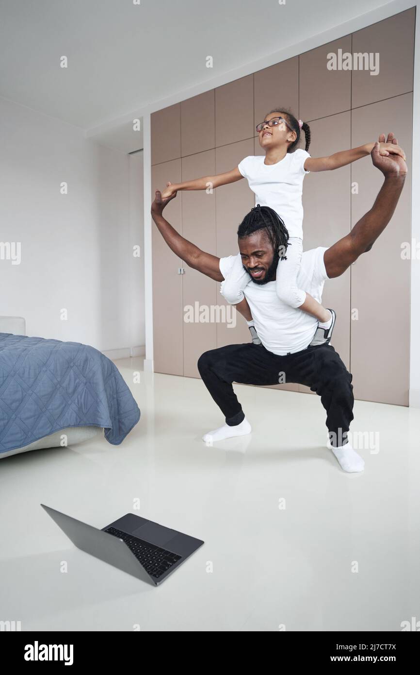 Adult african american man crouches with sitting daughter on his neck ...