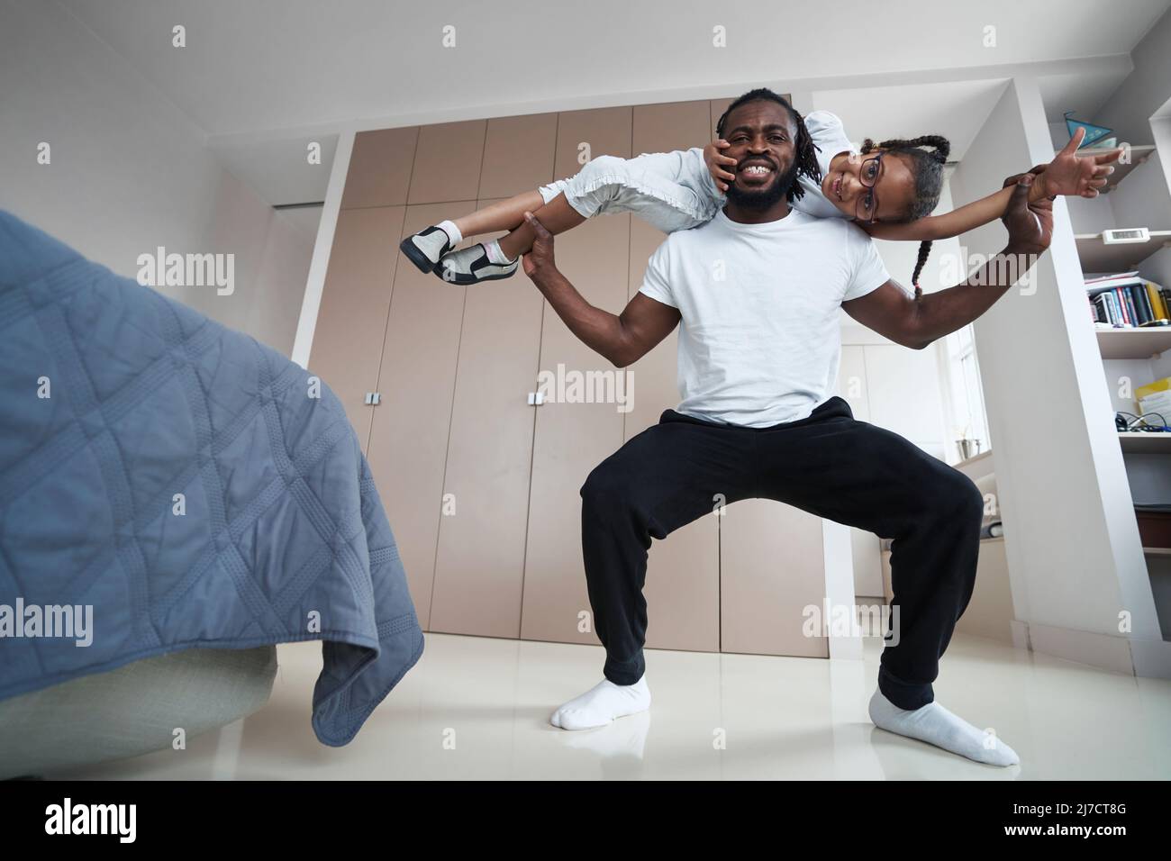 Adult African American father crouches with his daughter on his neck ...