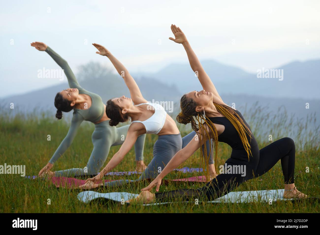 Side view of young girls doing crescent variation of warrior pose in ...