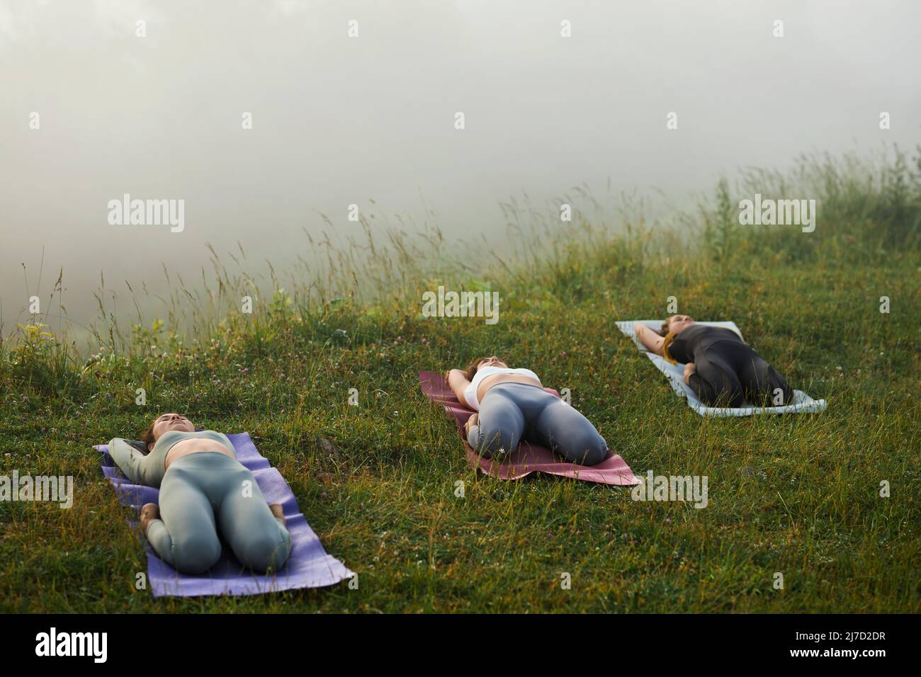 Side view of females lying down bending backwards, placing palms behind ...